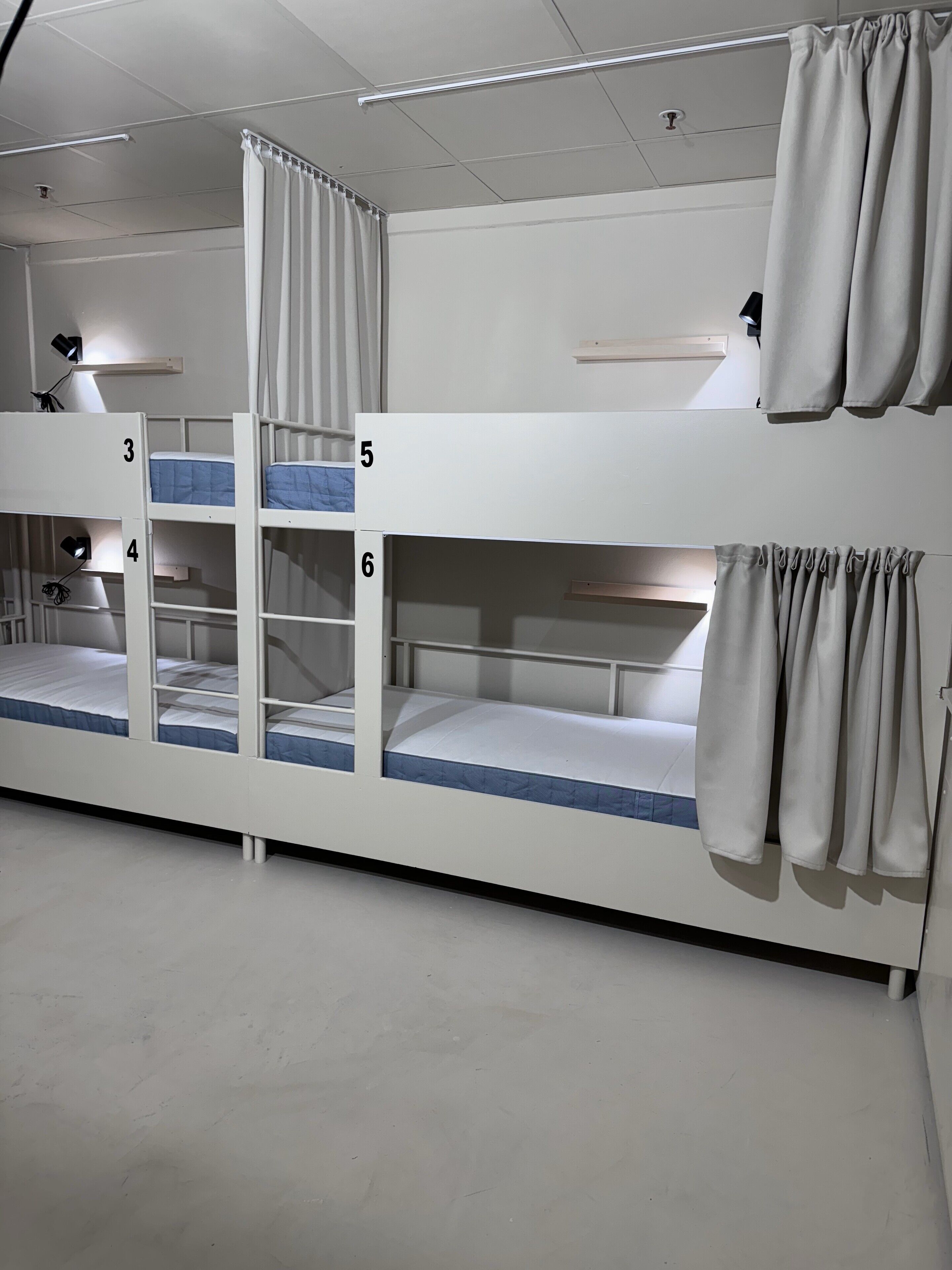 Quarto com beliche triplo, numerado de 3 a 6, e uma escrivaninha com luminária.