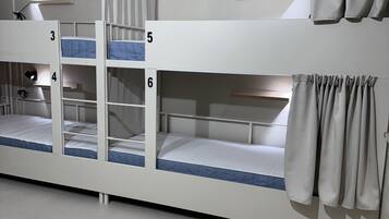 Quarto com beliche triplo, numerado de 3 a 6, e uma escrivaninha com luminária.