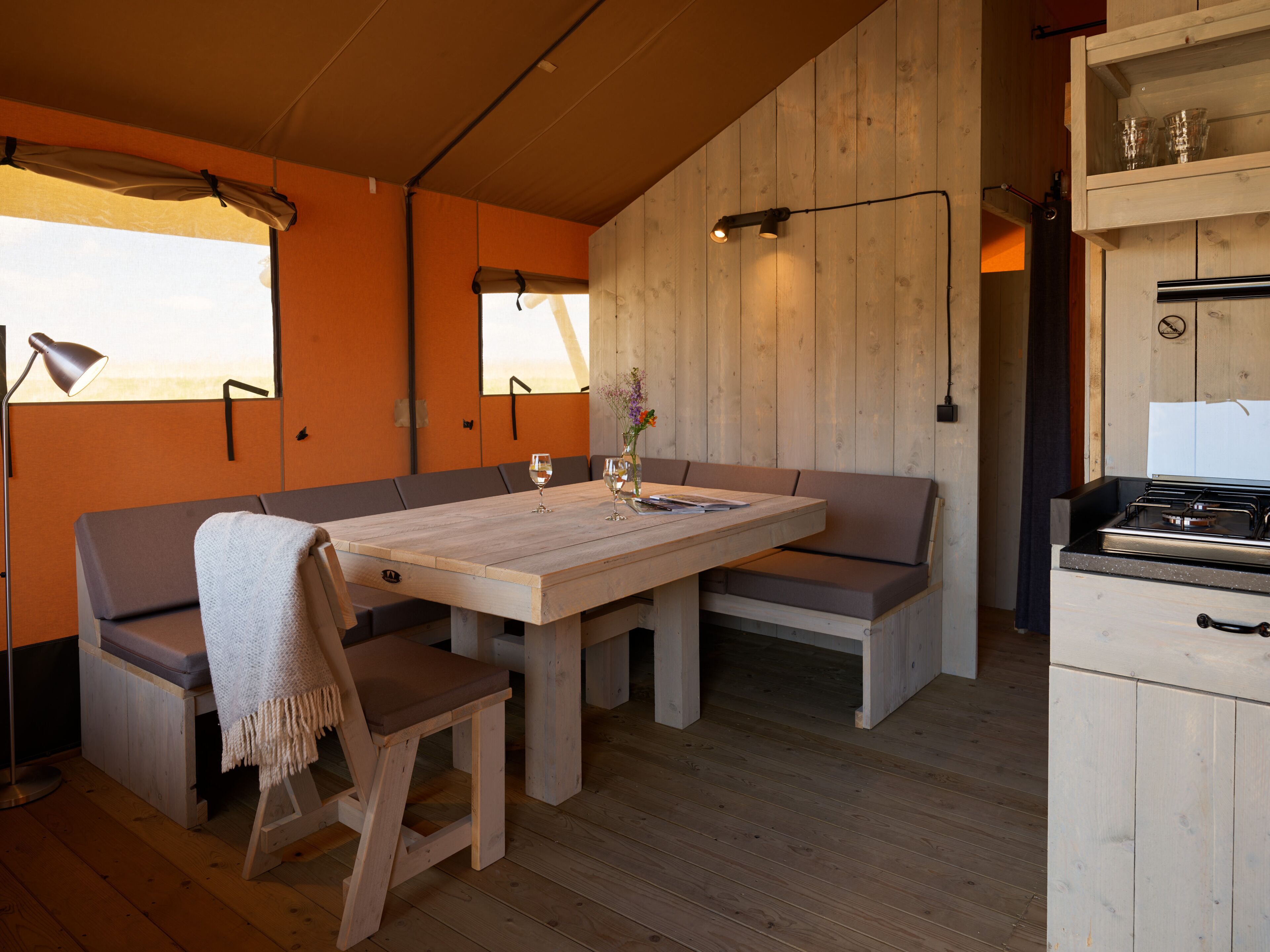 Interior acolhedor de uma cabana com uma mesa de jantar de madeira, bancos e uma área de cozinha com fogão.