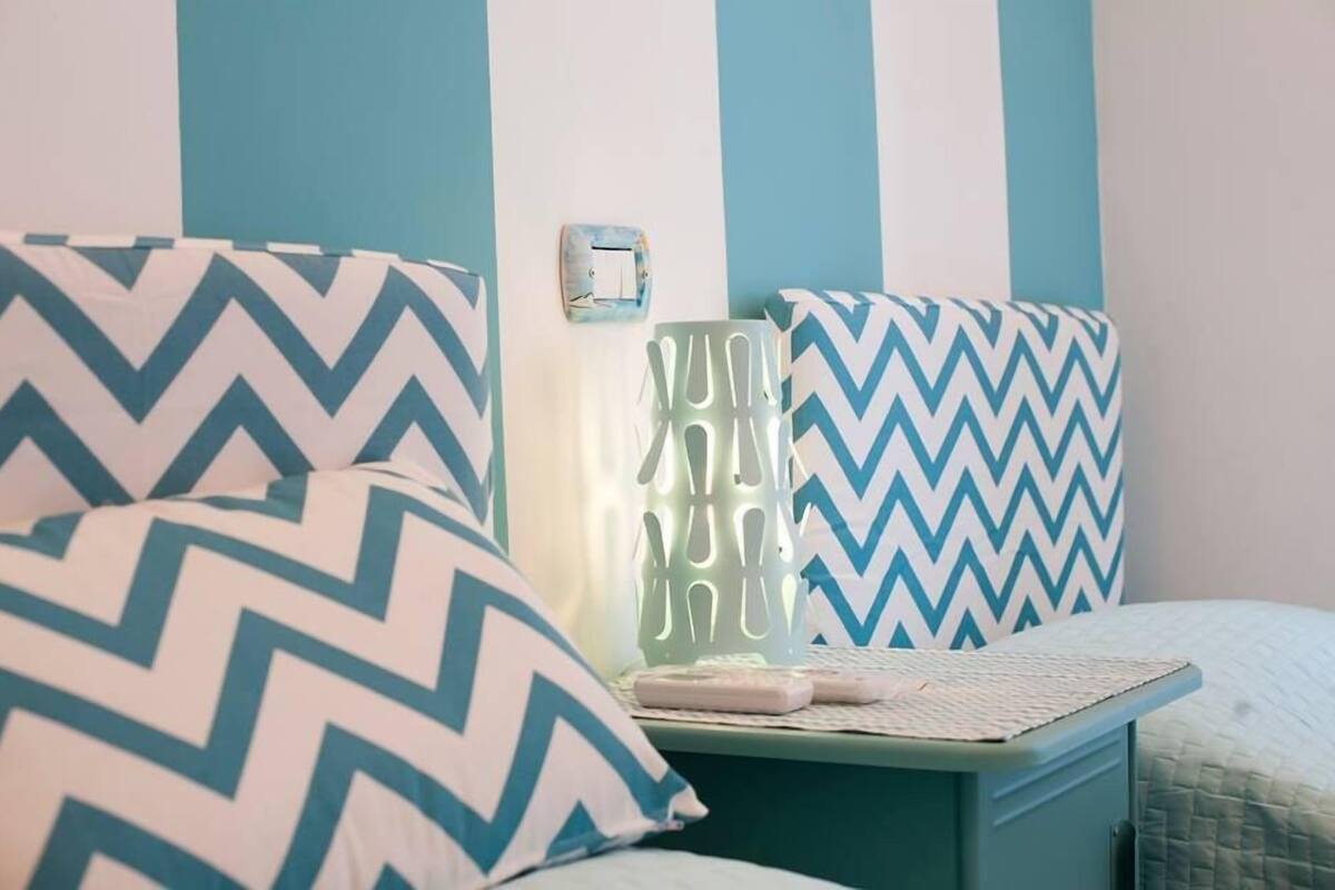 Quarto com cama, almofadas, mesa de cabeceira e abajur.