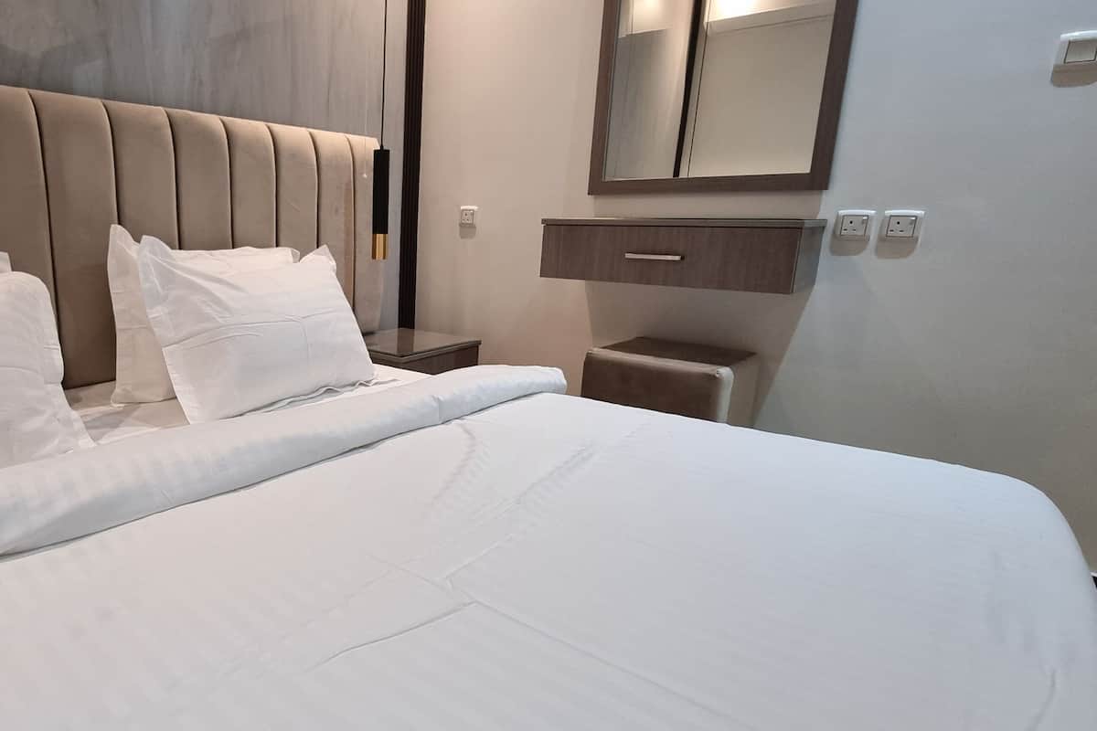 Cama bem arrumada com lençóis brancos e cabeceira acolchoada.