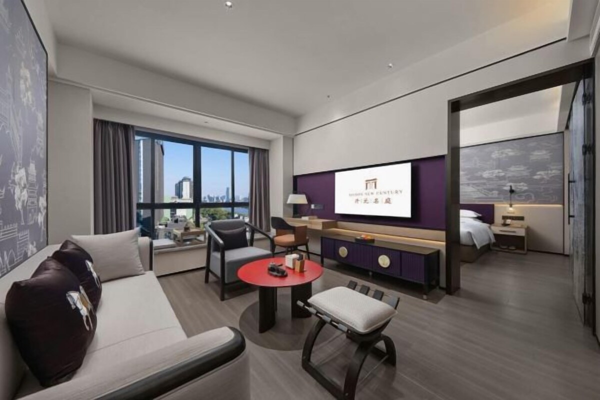 Quarto de hotel moderno com sofá, cadeiras, uma mesa pequena, cama e tela de TV.
