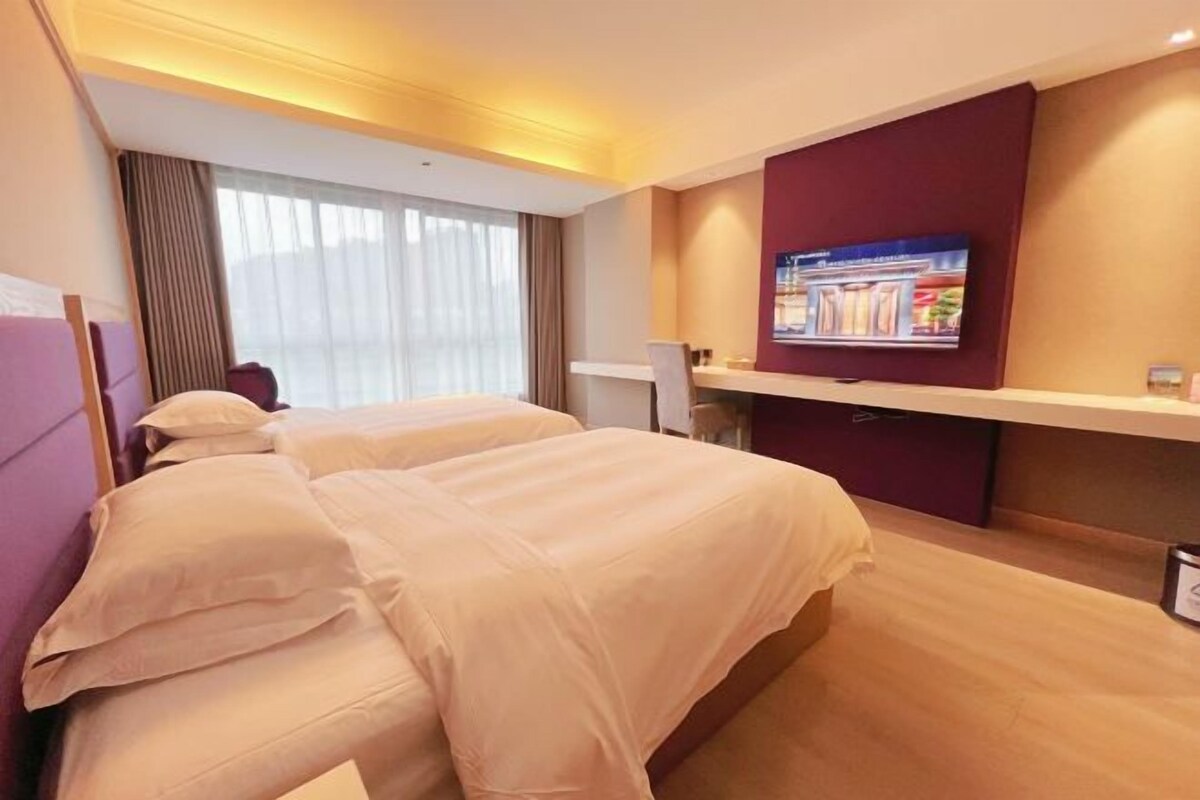 Quarto de hotel com duas camas, televisão e escrivaninha.