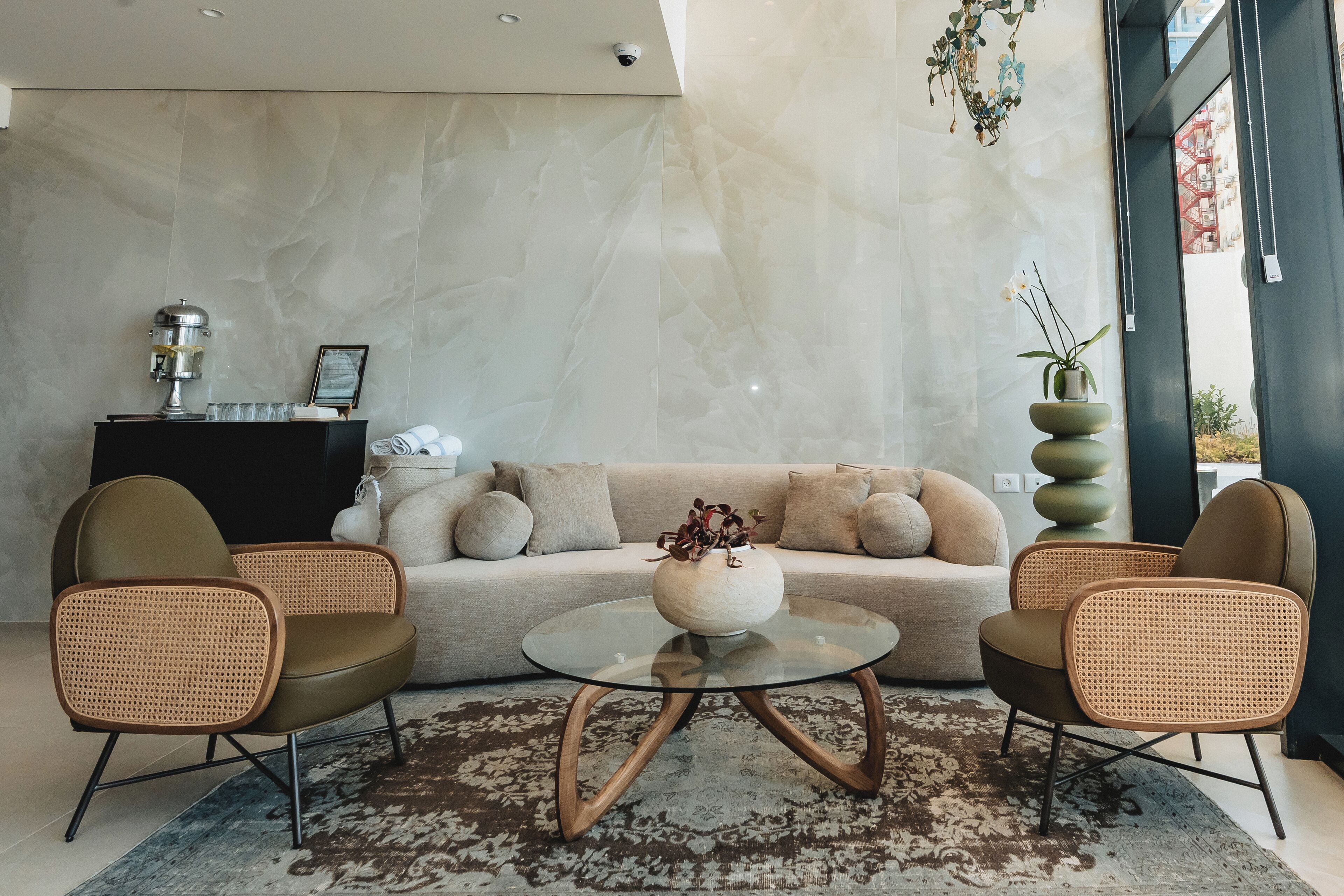 Uma sala de estar moderna com um sofá, duas cadeiras de vime, uma mesa de centro de vidro e um vaso decorativo.