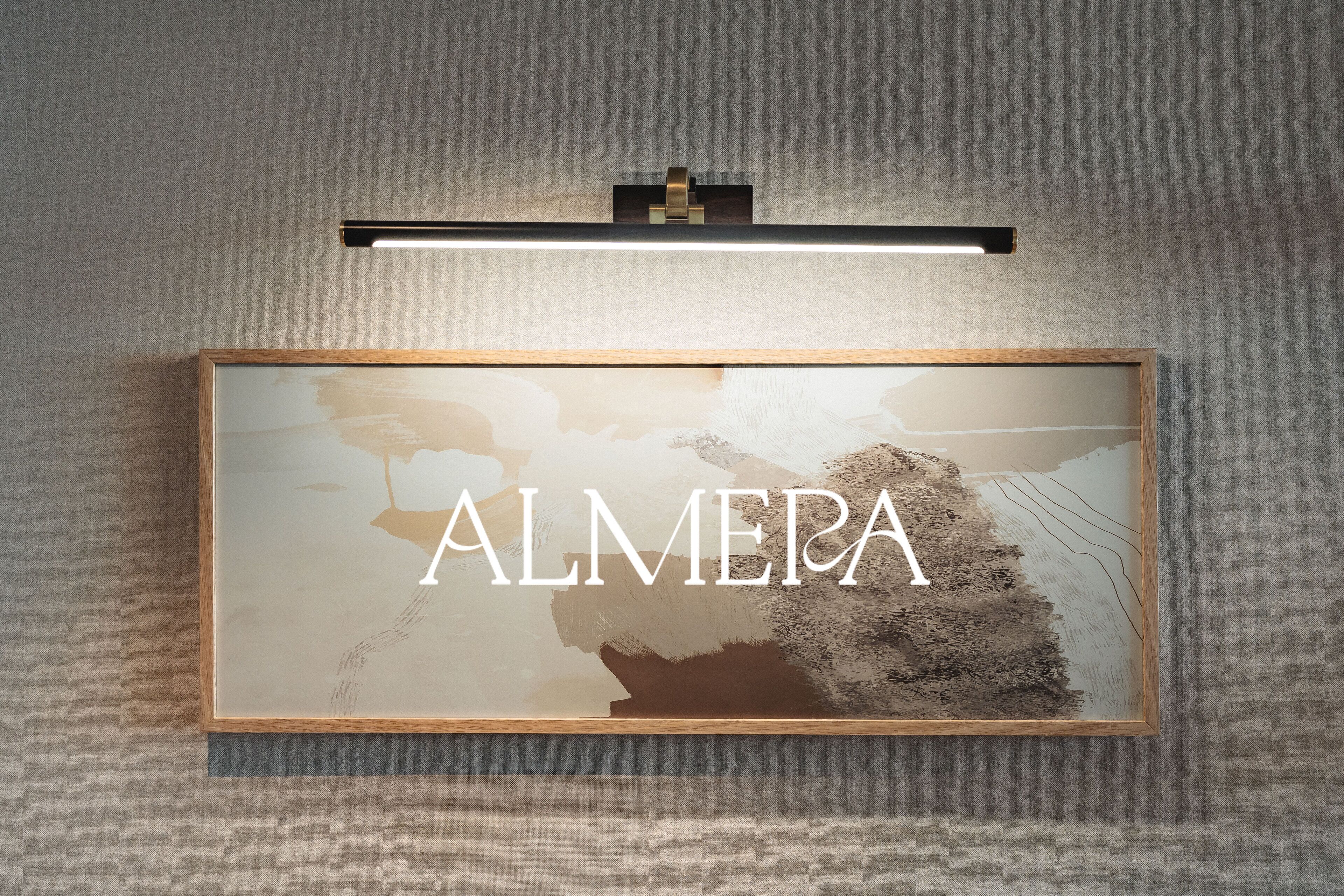 Obra de arte emoldurada com a palavra "ALMERA" numa parede texturizada, iluminada por um candeeiro de teto.
