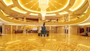 Um hall amplo com um lustre central, um balcão de recepção e uma estátua.
