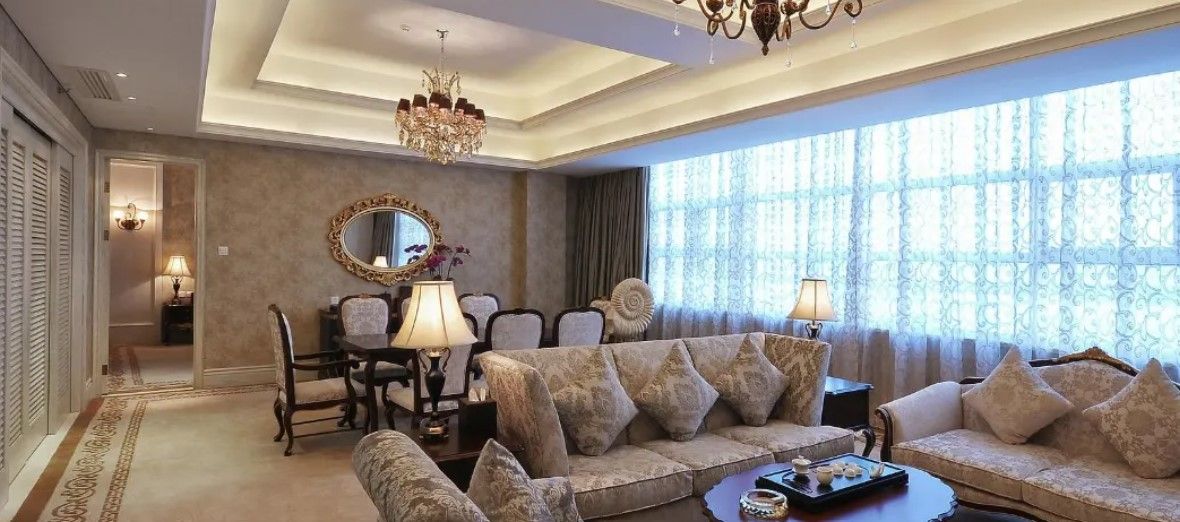 Uma sala de estar ampla com um amplo sofá, uma área de jantar com cadeiras e uma mesa, e um candelabro.