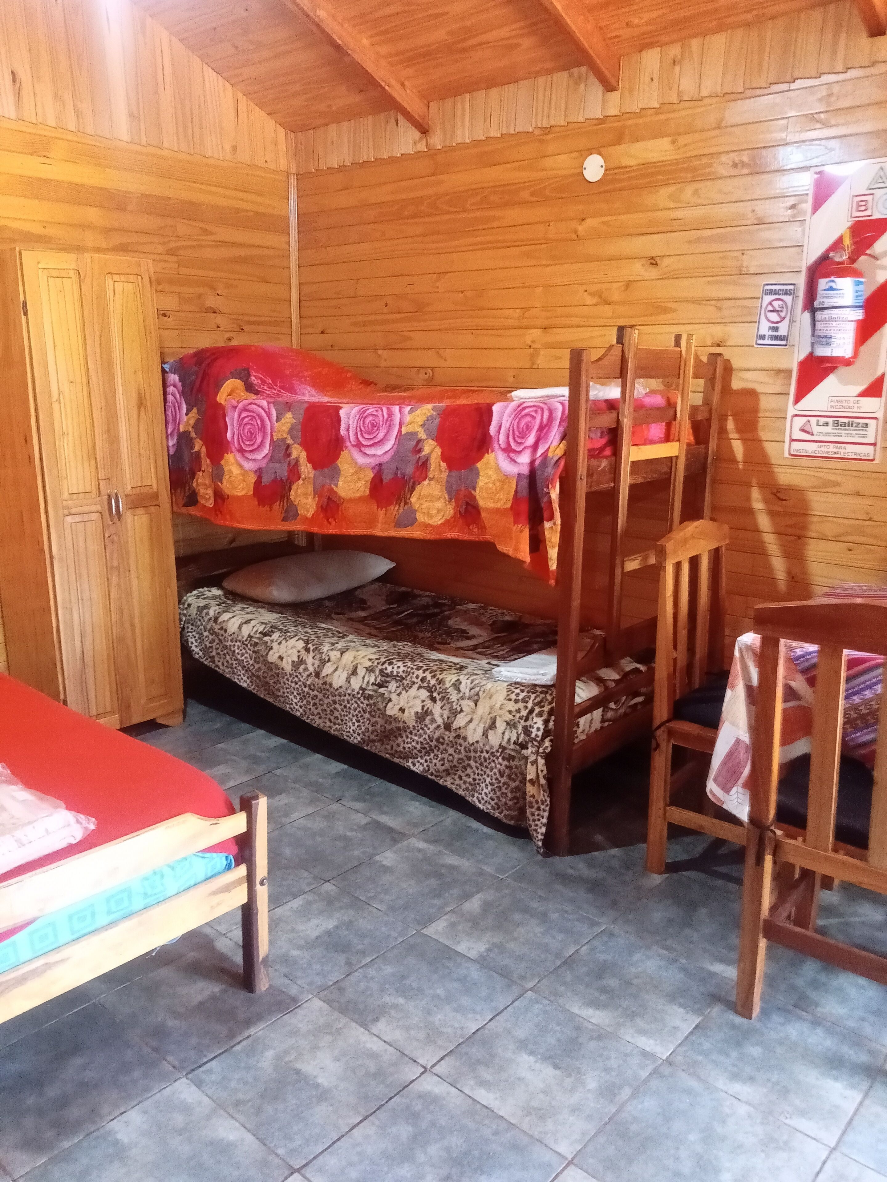 Quarto de cabana de madeira com beliche, uma mesinha e uma cadeira.