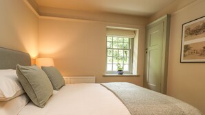 Quarto com cama, almofadas, luminária, janela com vista para o verde e porta.