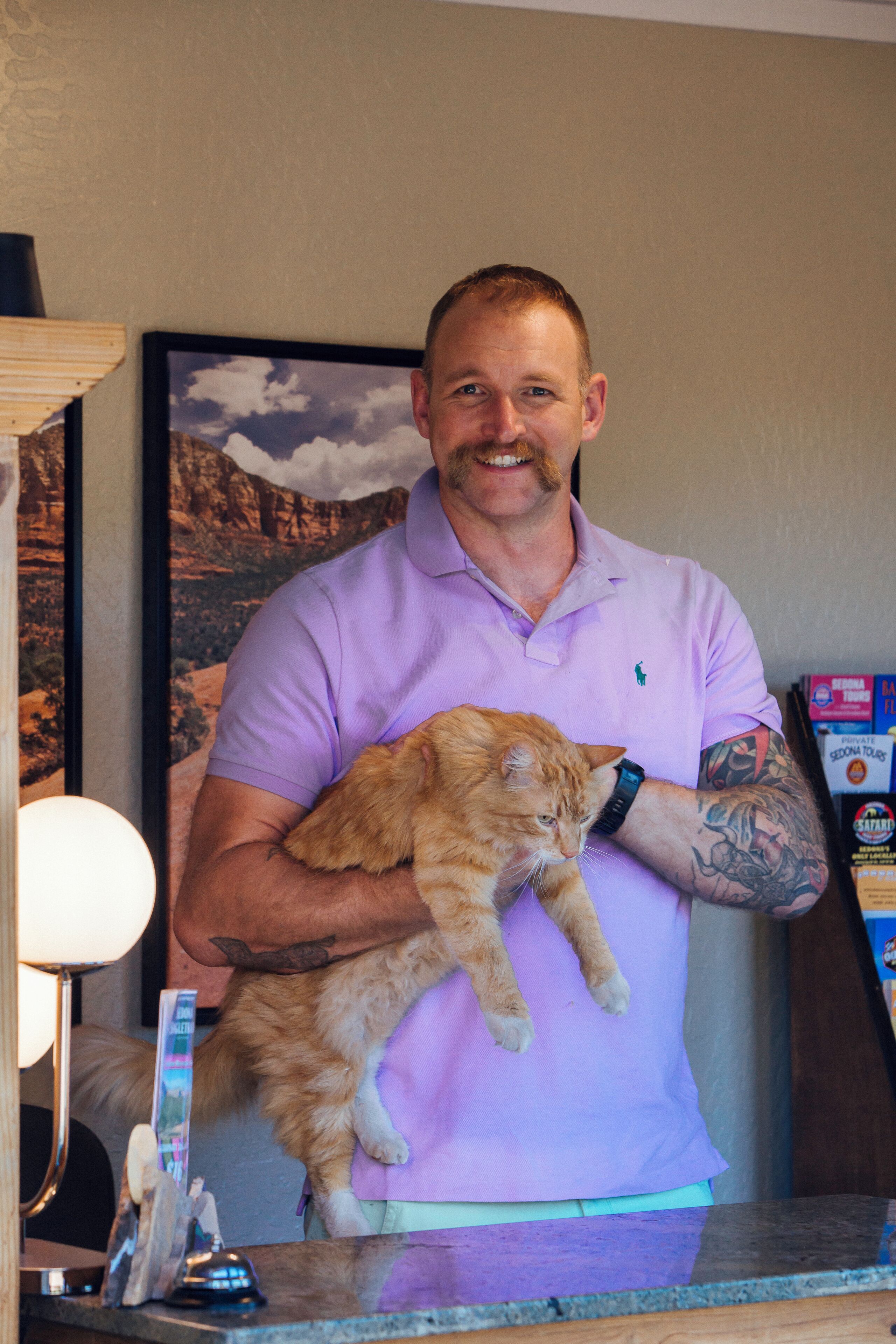 Um homem segurando um gato em um quarto com pôster de paisagem montanhosa na parede.