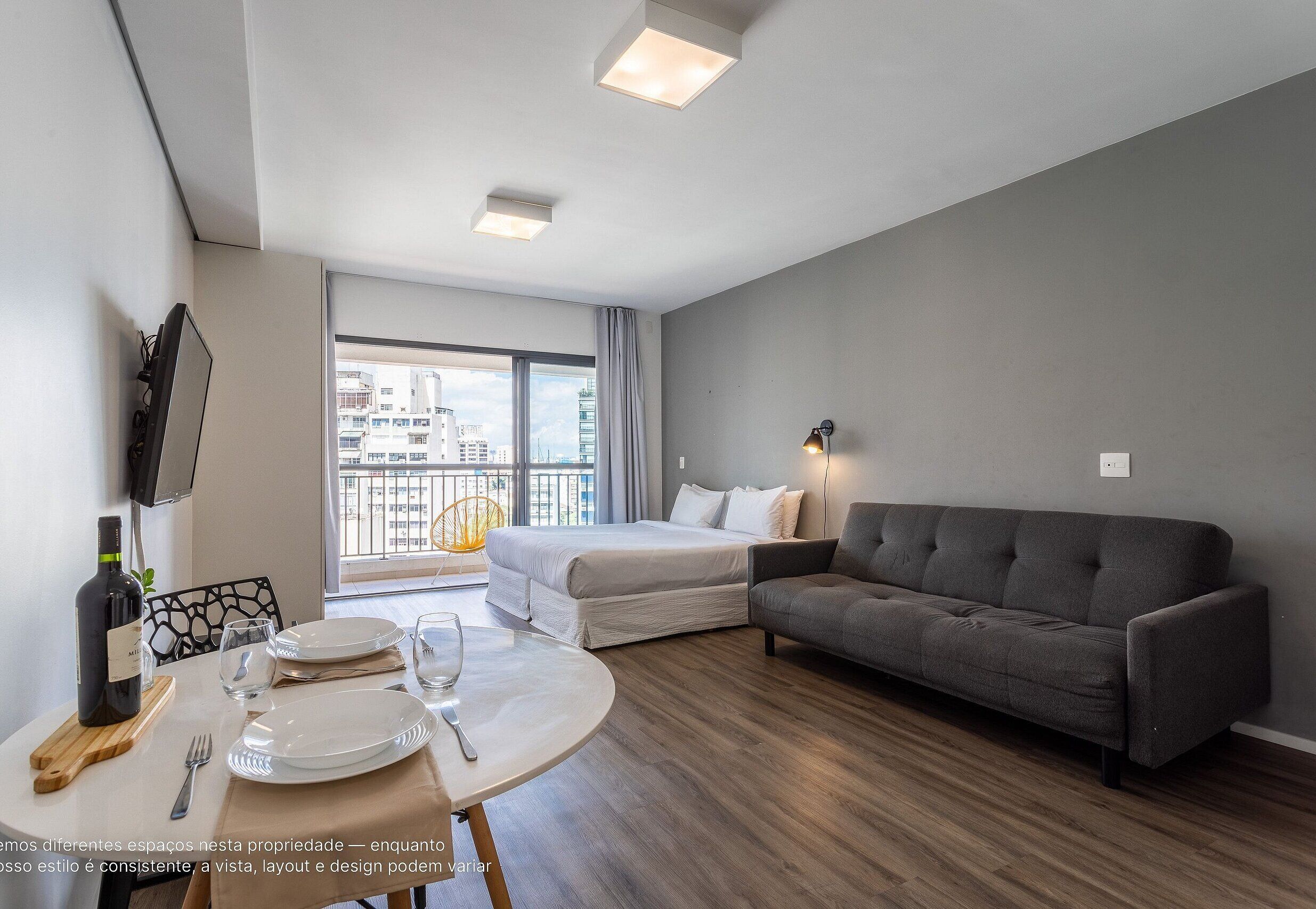 Quarto de hotel moderno com cama, sofá, mesa de jantar e uma garrafa de vinho.