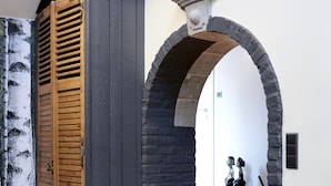 Um corredor com porta de madeira, um arco de pedra e escadas que levam a um andar superior.