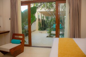 Um quarto com uma cama, uma cadeira de madeira com almofada e uma porta de vidro deslizante para um alpendre com plantas e uma mesa pequena.