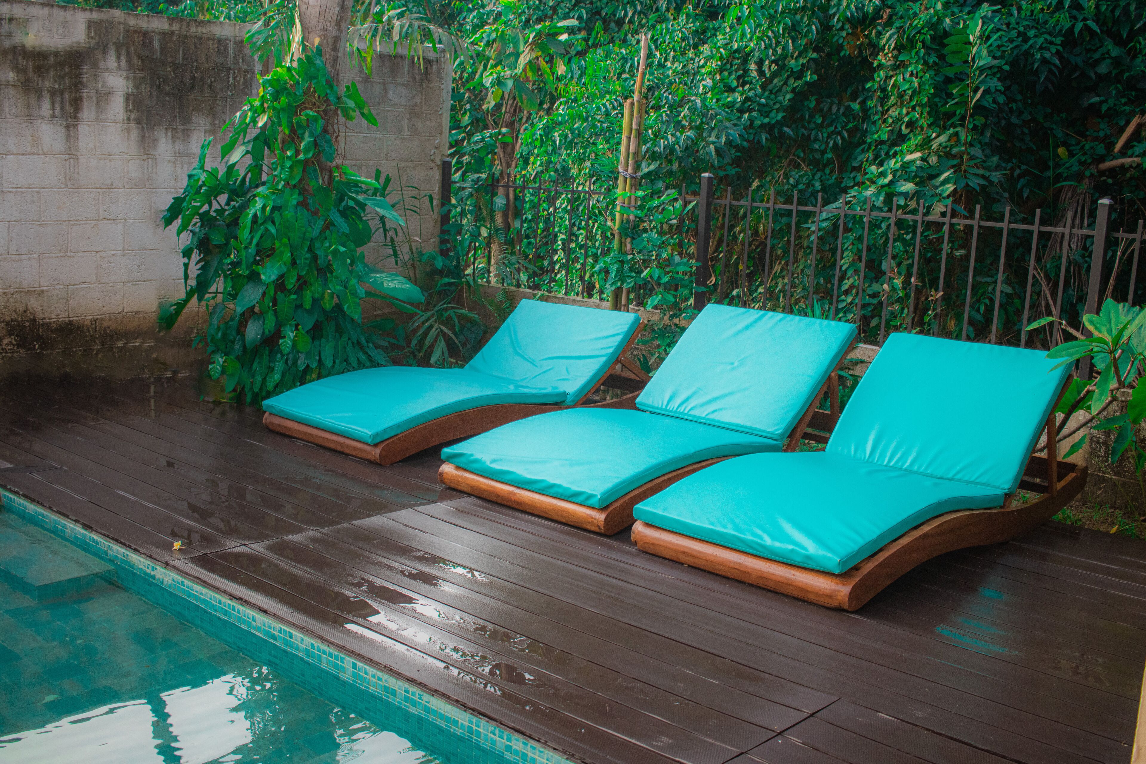 Área de piscina com três espreguiçadeiras e deck de madeira.