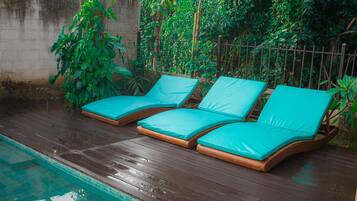 Área de piscina com três espreguiçadeiras e deck de madeira.