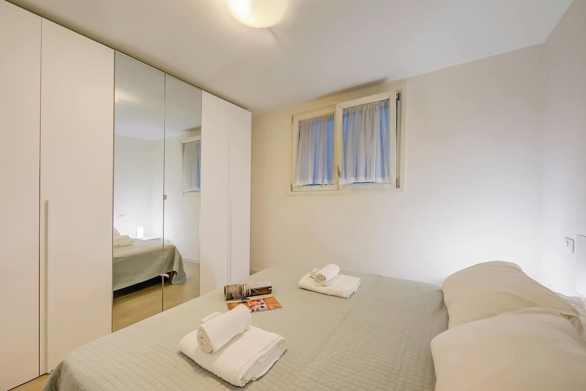 Um quarto com cama, guarda-roupa e janela com cortinas.