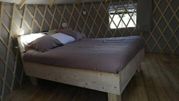 Uma cama de solteiro em quarto de madeira com parede treliçada e janela.