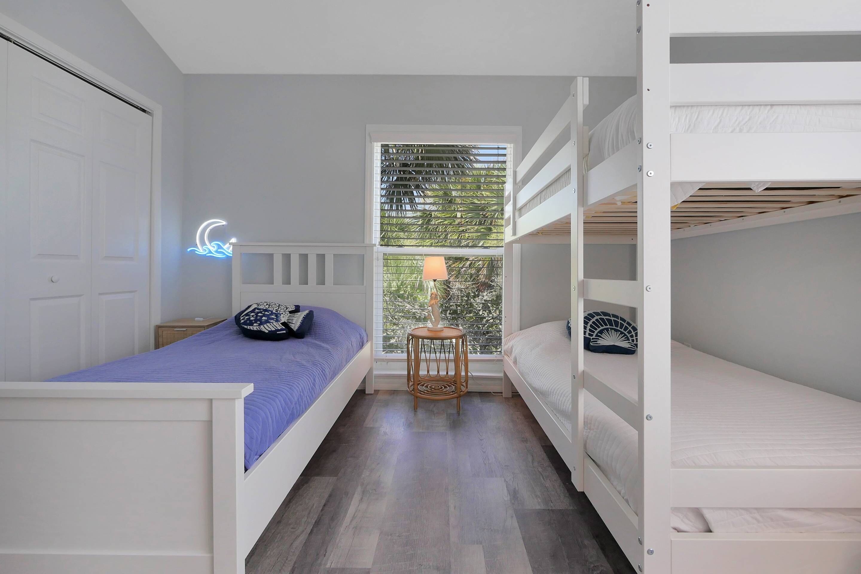 Quarto com uma cama de solteiro, janela com persianas, mesa de cabeceira e uma luminária.