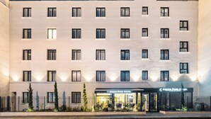 Um hotel com vários andares, fachada plana, janelas regularmente espaçadas e entrada central com uma placa indicando "Green Park Hotel".