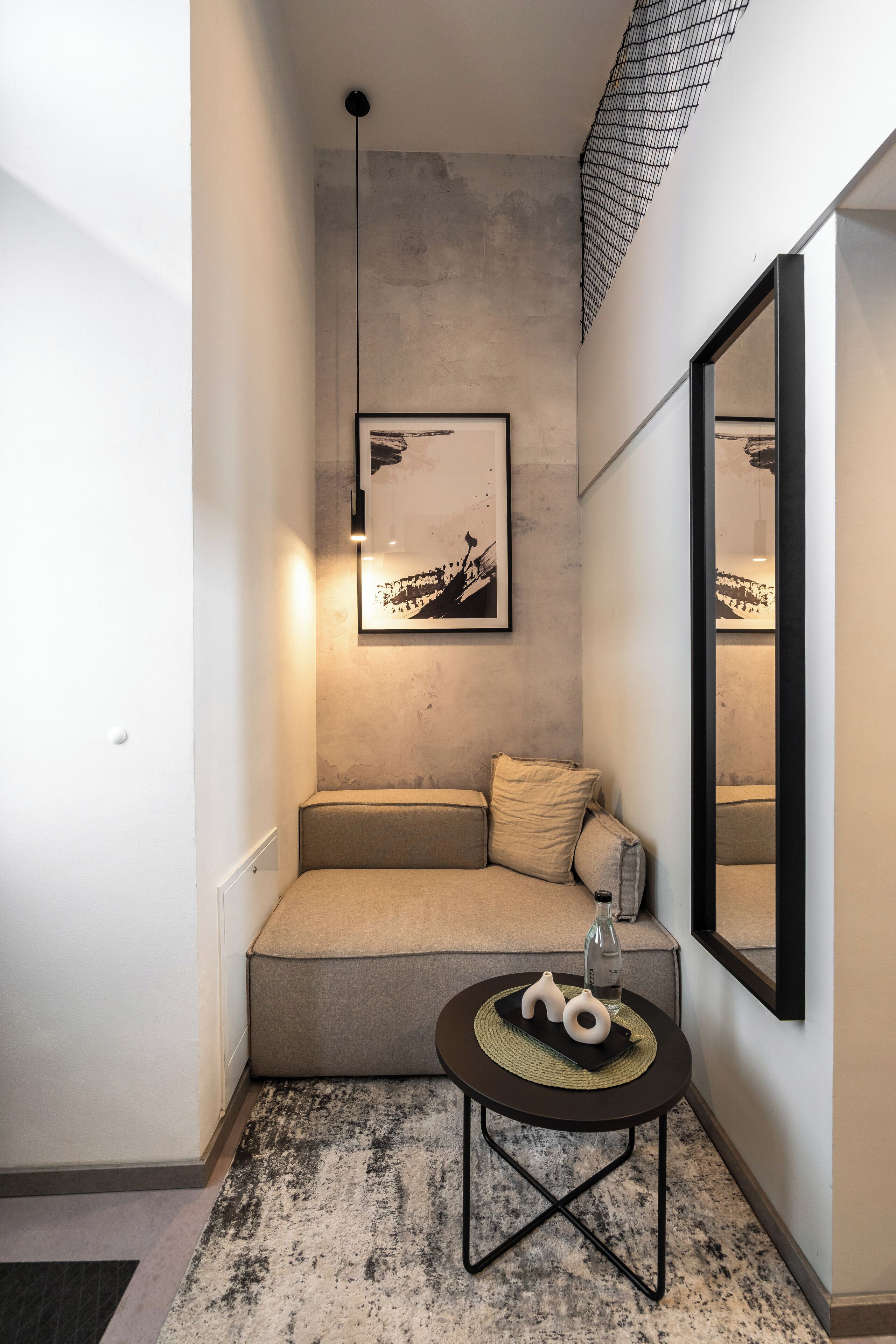 Um interior moderno com um sofá, uma mesinha redonda com objetos decorativos, uma obra de arte emoldurada e um espelho grande.