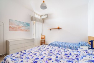 Quarto com cama, cadeira, prateleira e luminária na parede.