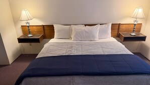 Cama bem arrumada com roupa de cama branca e azul, duas luminárias de cabeceira e cabeceiras de madeira.