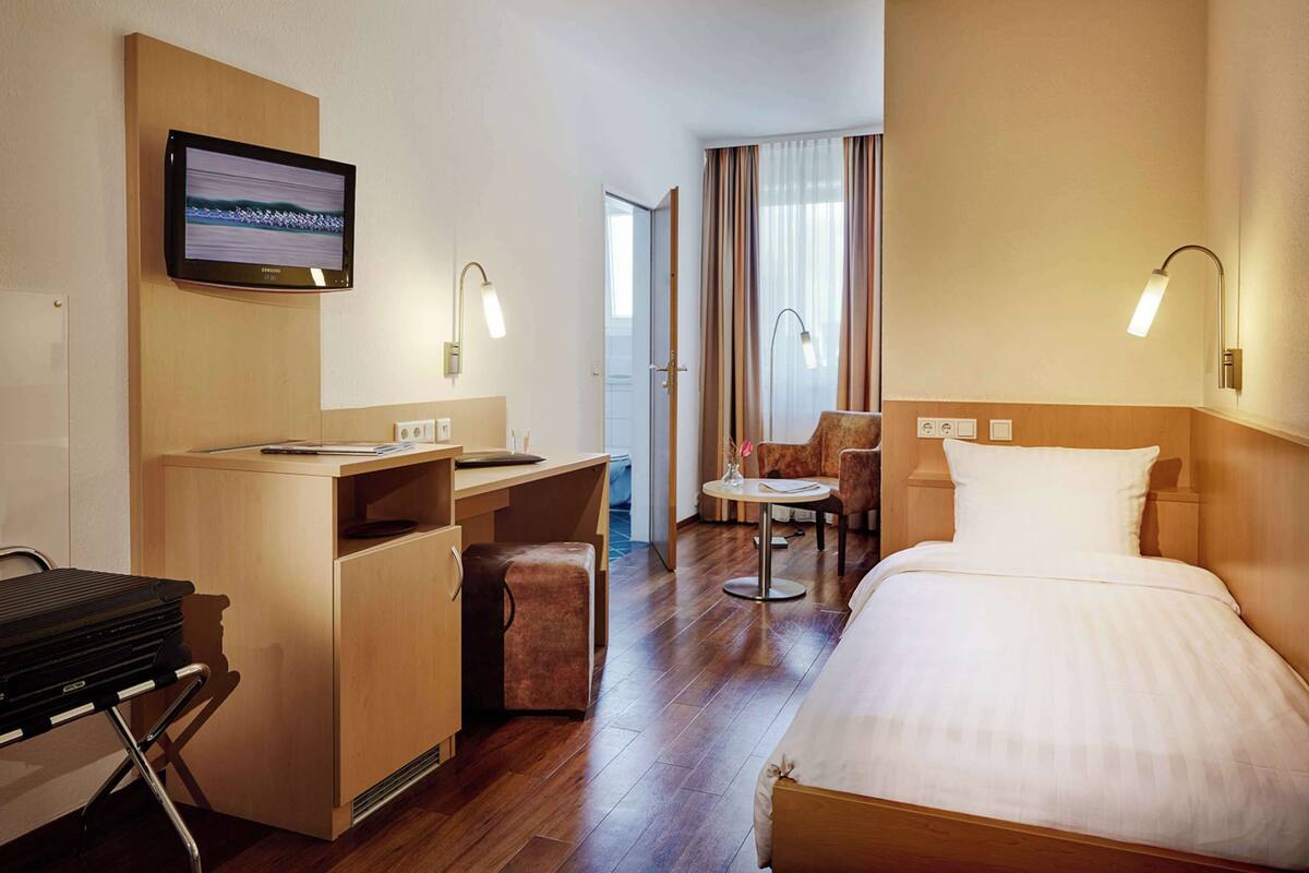 Quarto de hotel com cama, escrivaninha, cadeira, televisão e uma pequena mesa.