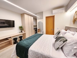Quarto moderno com cama, TV, guarda-roupa e escrivaninha.