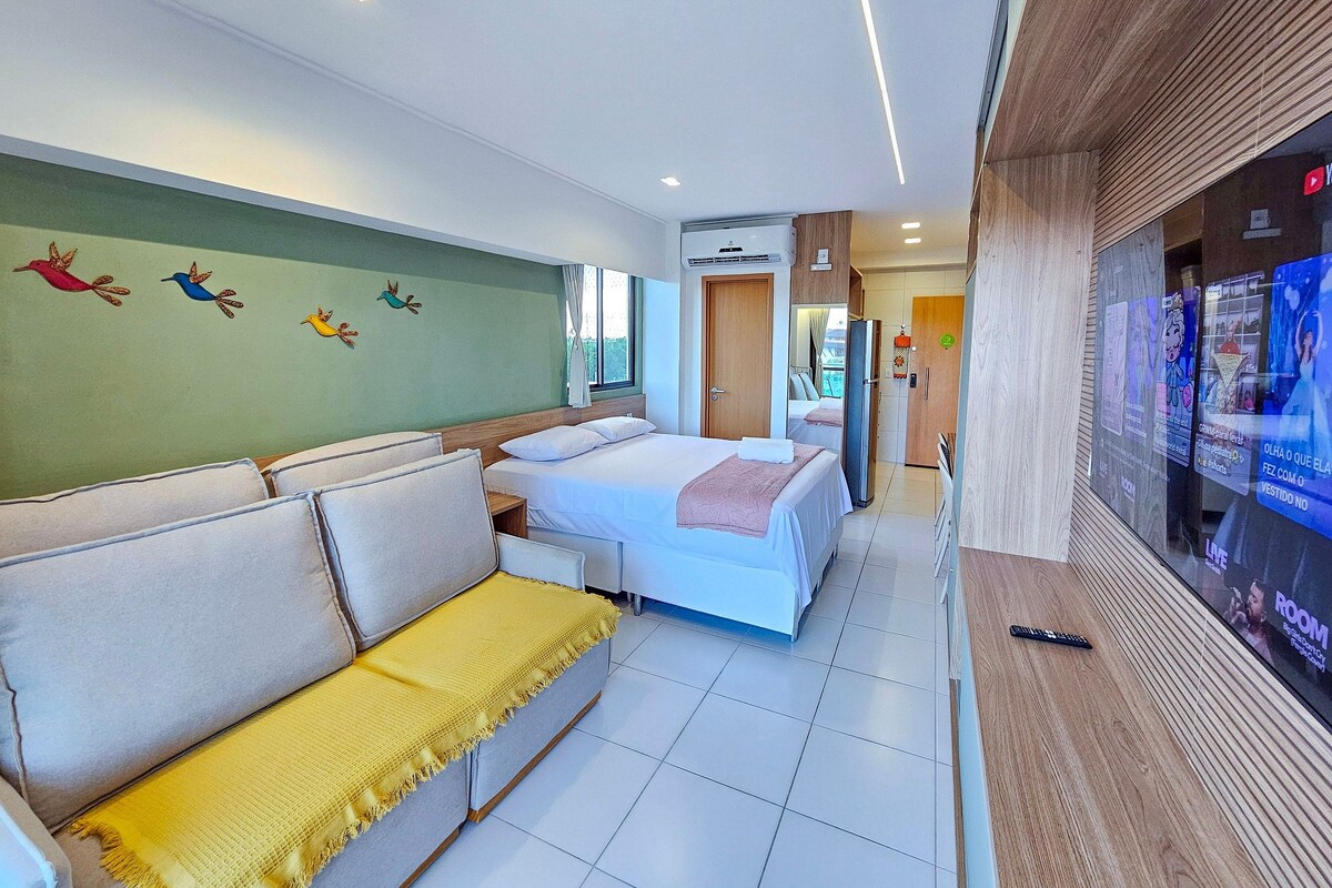 Quarto de hotel com uma cama, um sofá, uma televisão e uma parede decorada com pássaros.