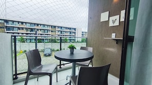 Varanda com mesa e cadeiras, um vaso de planta e vista para um estacionamento e edifícios.
