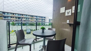 Varanda com mesa e cadeiras, um vaso de planta e vista para um estacionamento e edifícios.
