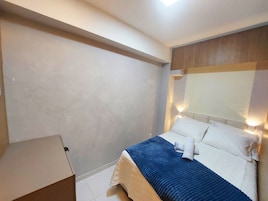 Quarto de hotel com uma cama, mesa de cabeceira e cabeceira iluminada.