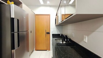 Uma cozinha compacta com geladeira, forno, pia e porta de madeira.