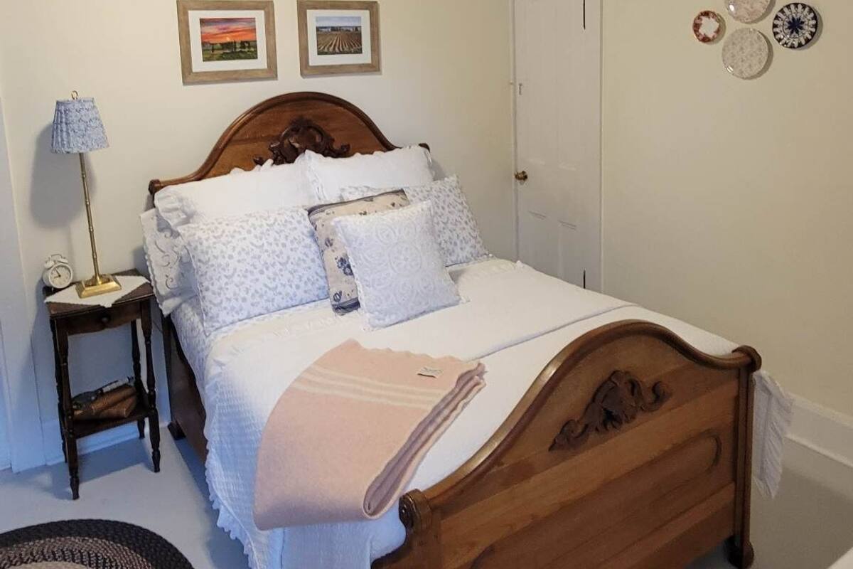Quarto com cama de madeira, mesa de cabeceira, abajur, quadros nas paredes e teto com padrão floral.