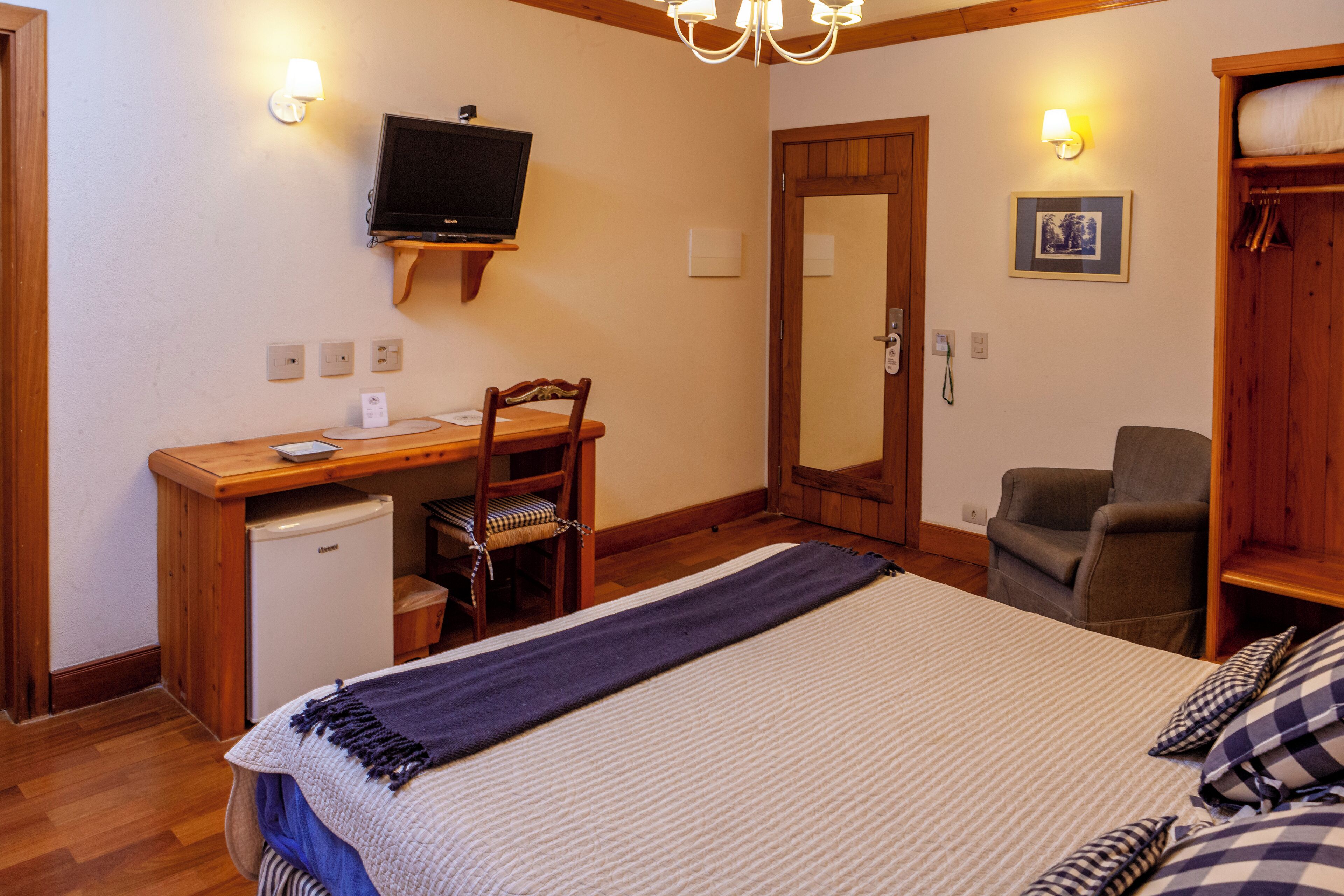 Um quarto com cama, escrivaninha, cadeira, televisão e guarda-roupa.
