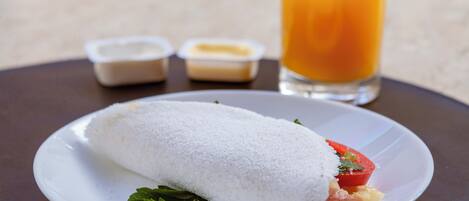 Um prato com um alimento enrolado, um copo de suco de laranja e dois pequenos recipientes sobre uma mesa.