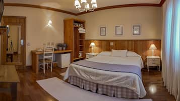 Quarto de hotel com secretária de madeira, cama com colcha xadrez, mesa de cabeceira com abajur e guarda-roupa.