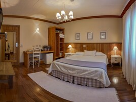 Quarto de hotel com secretária de madeira, cama com colcha xadrez, mesa de cabeceira com abajur e guarda-roupa.