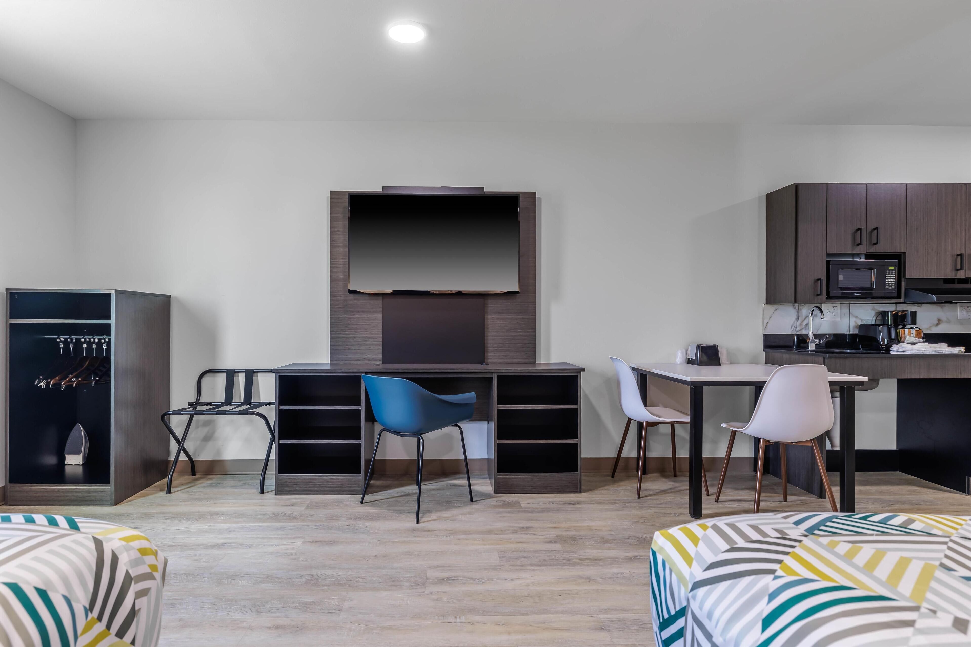 Quarto de hotel moderno com cozinha compacta, cama com roupa de cama listrada e duas cadeiras.