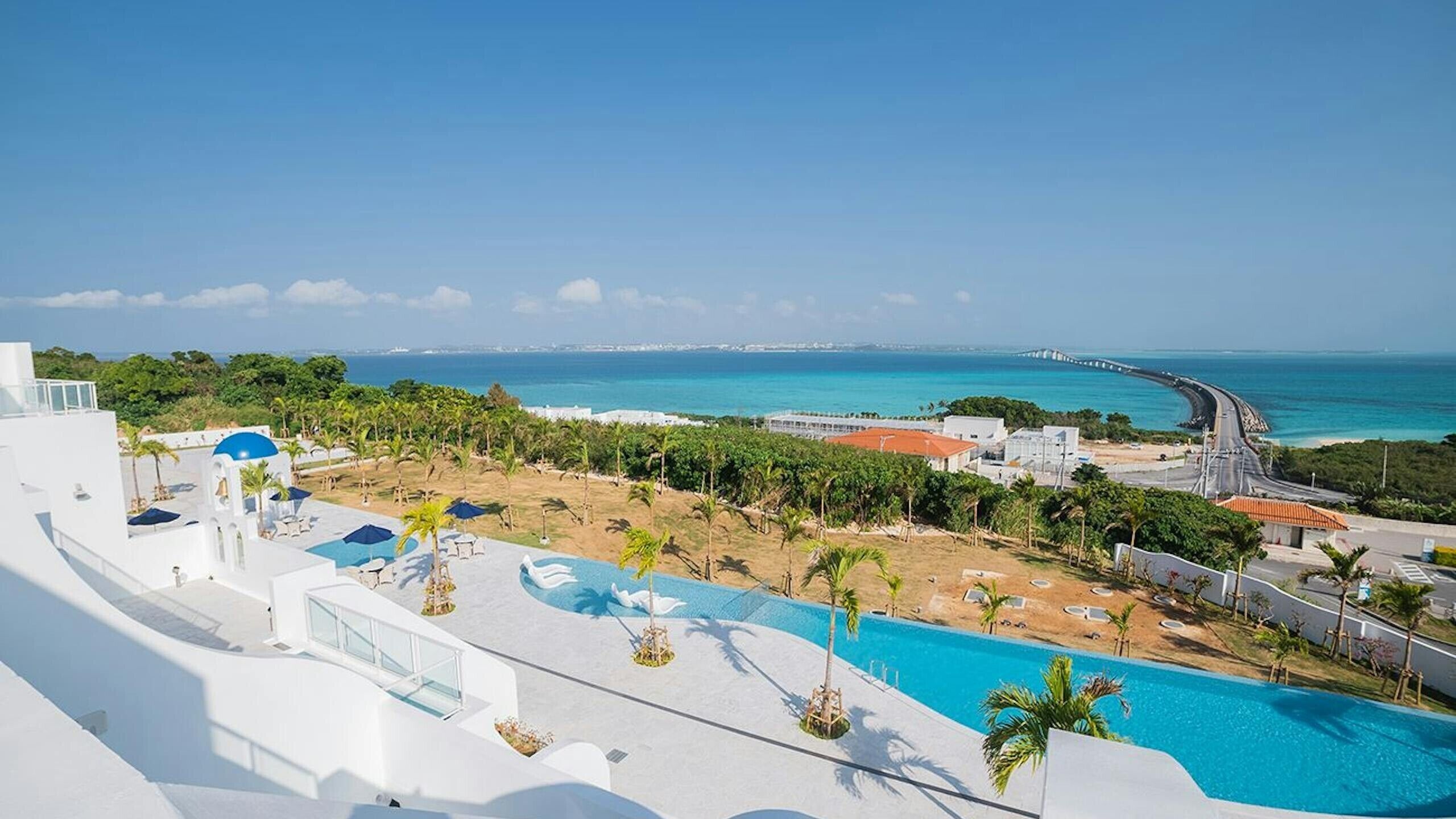Um resort com uma piscina grande, palmeiras e vista para o oceano e uma ponte.