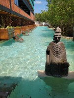 Uma estátua em uma piscina translúcida, com estruturas de madeira e um edifício ao fundo.