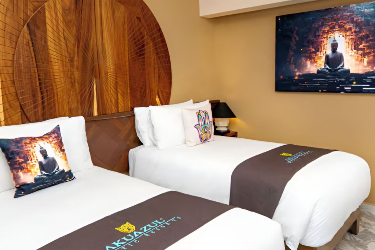 Quarto de hotel com duas camas, uma grande cabeceira de madeira, uma televisão na parede e uma estátua de Buda.