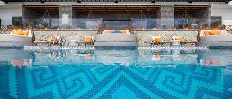 Uma piscina com padrão geométrico de azulejos, rodeada por espreguiçadeiras e almofadas.