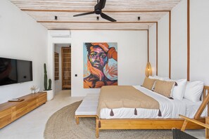 Quarto moderno com cama, televisão, pintura e ventilador de teto.