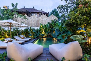 Uma área de piscina com espreguiçadeiras e guarda-sóis, cercada por vegetação tropical exuberante.