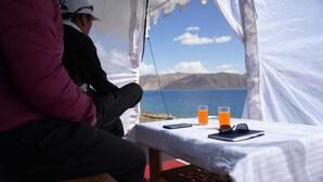 Uma tenda com uma mesa posta para dois, dois copos de suco de laranja e um smartphone sobre a mesa.