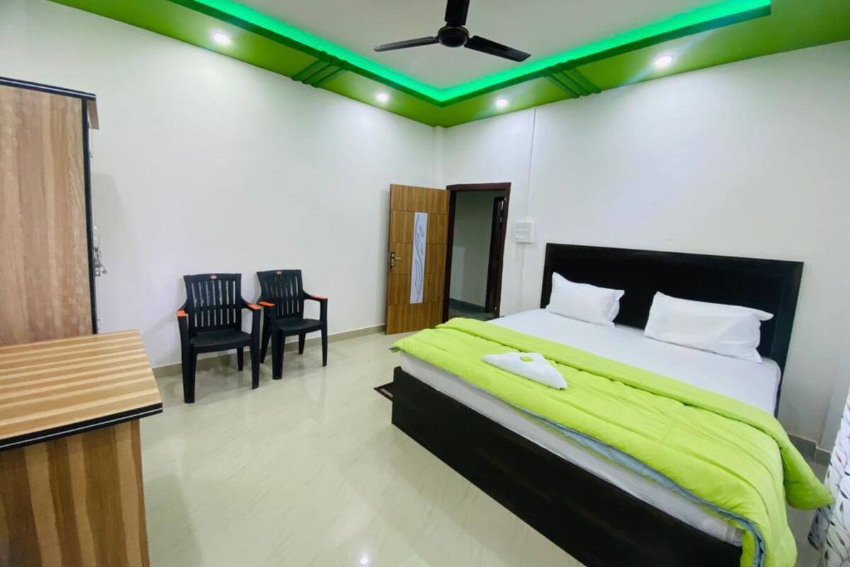 Quarto de hotel com uma cama, duas cadeiras, uma escrivaninha e um ventilador de teto.