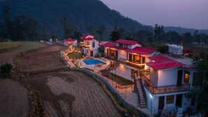 Um resort com vários andares, piscina, edifícios com telhados vermelhos e montanhas ao fundo.