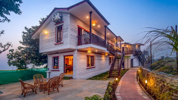 Uma casa de dois andares com varanda, escadaria e um espaço de pátio com cadeiras.