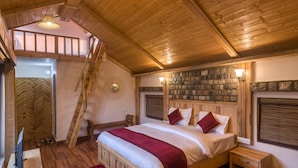 Quarto com teto de madeira, parede de pedra, cama com roupa de cama vermelha e branca, mesa de cabeceira e tapete vermelho.